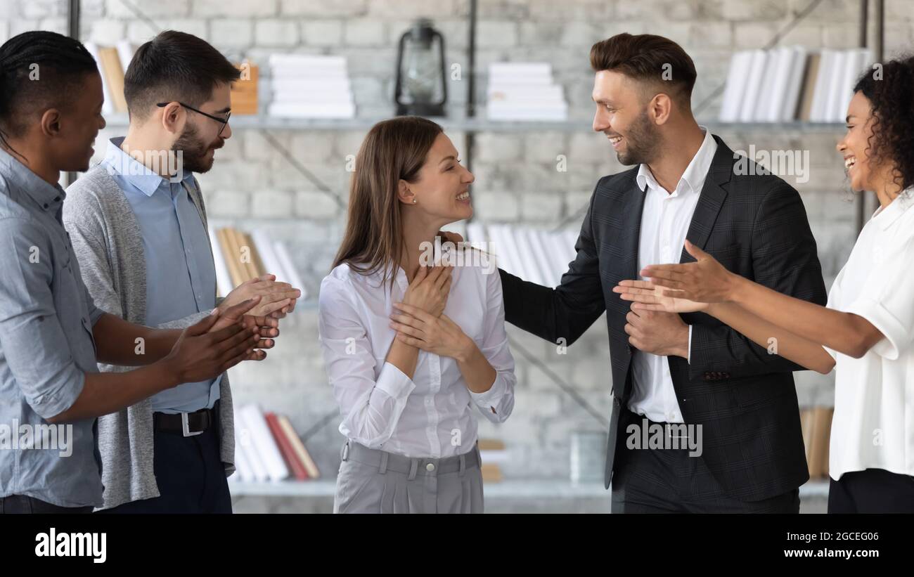 Smiling diverse employees greeting excited female colleague with ...