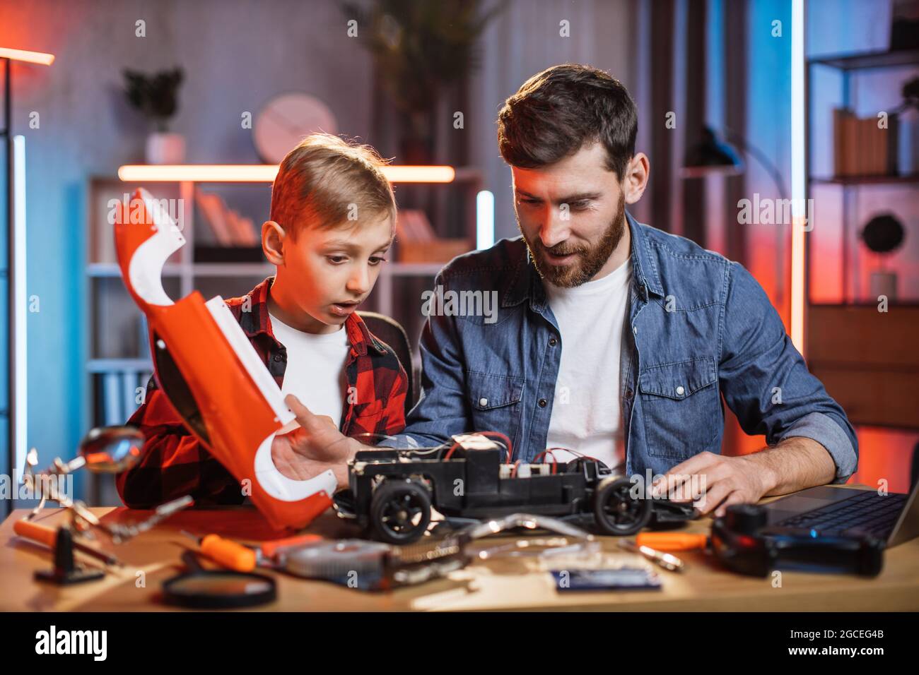 Focused bearded man and little boy sitting together at table and ...