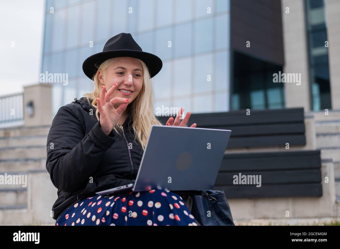 Young woman speaks sign language on a video call on a laptop outdoors ...