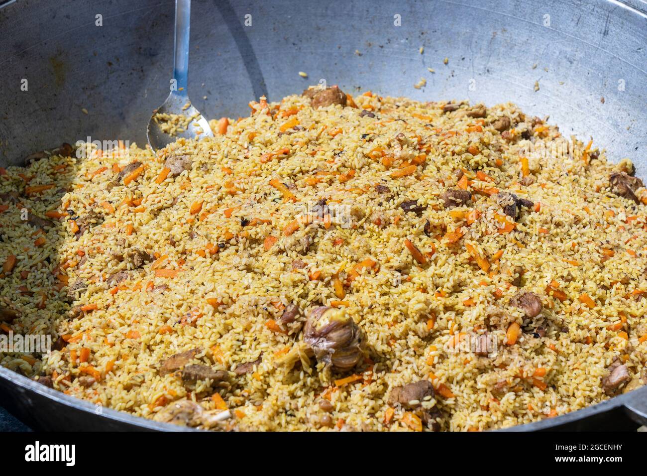 Cooking of traditional pilaf in big cauldron on the street food market ...