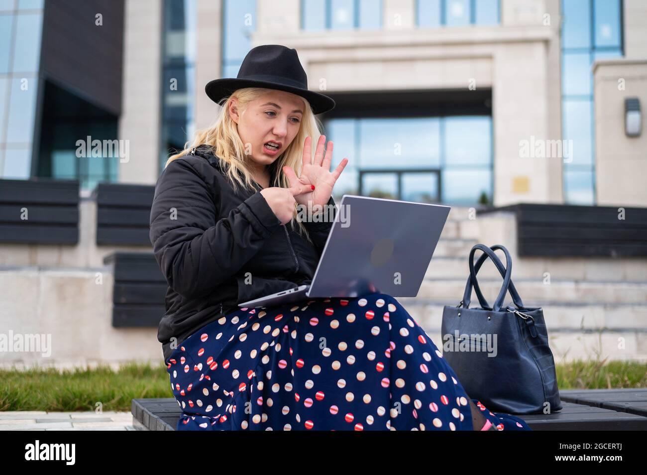 Young woman speaks sign language on a video call on a laptop outdoors ...