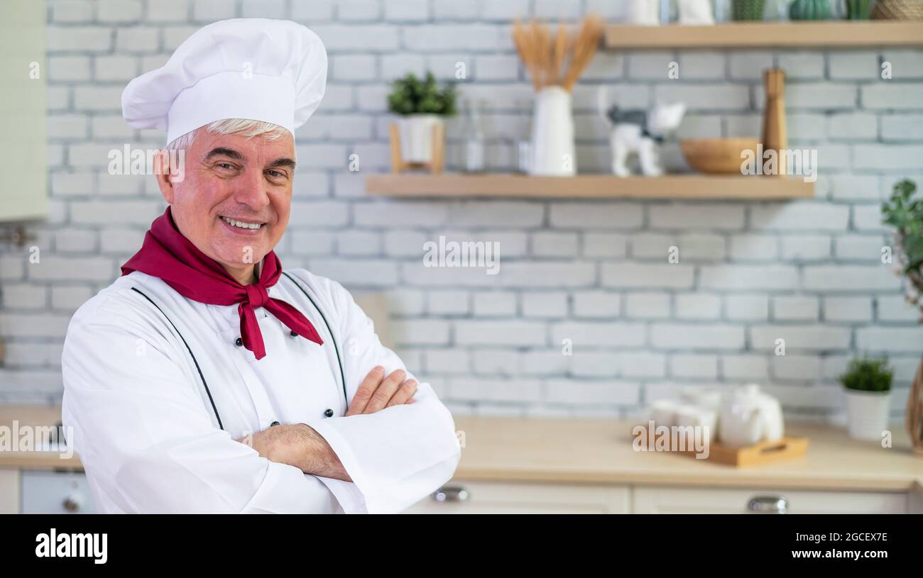 Portrait of a smiling elderly chef standing in the kitchen with his ...
