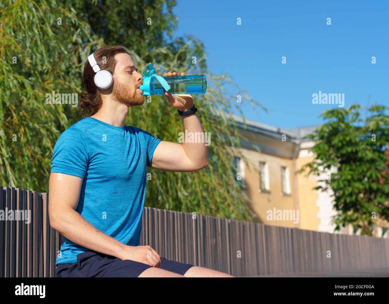 Young thirsty sportsman drinking fresh water from bottle while running ...
