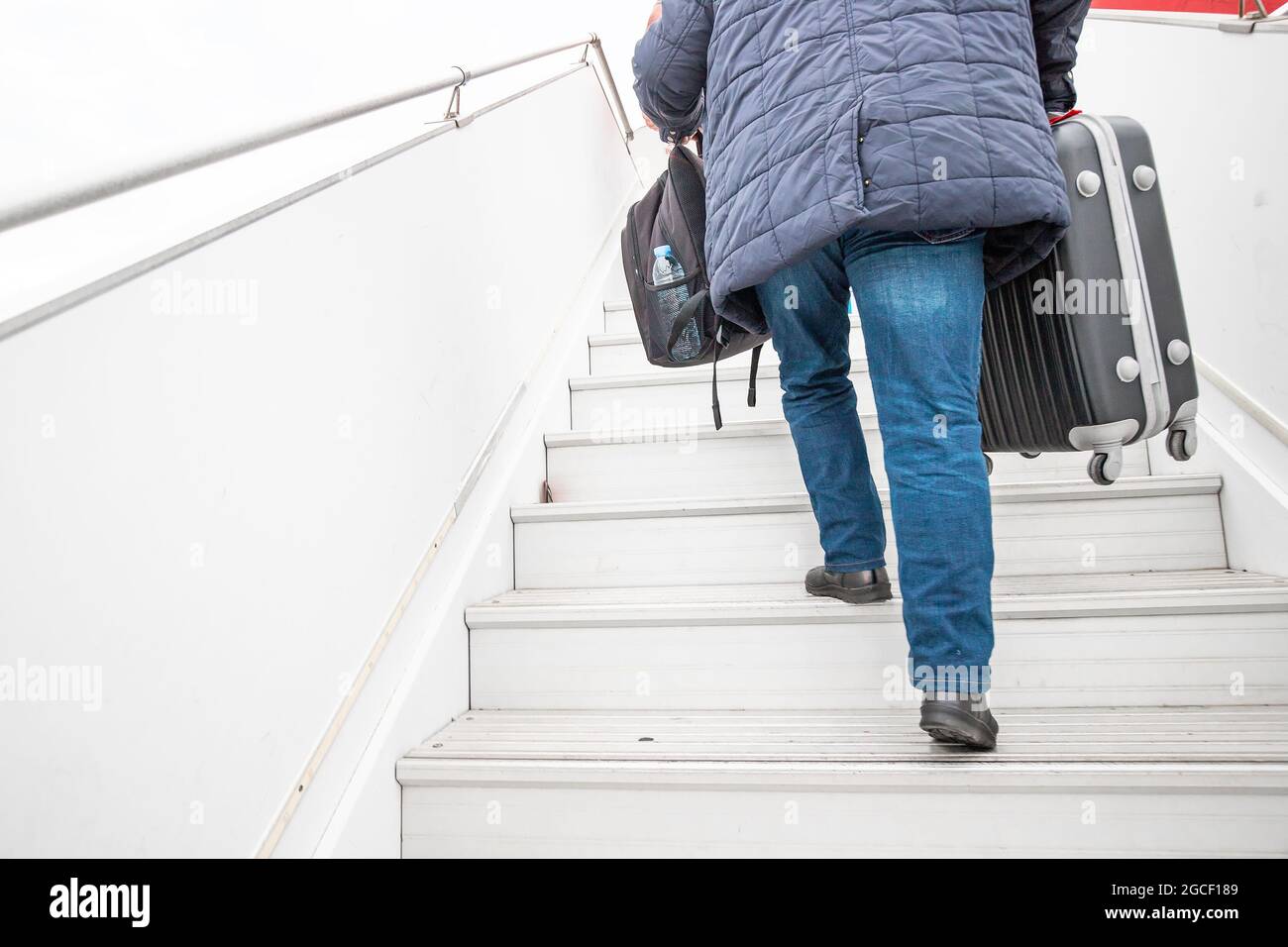 Senior passenger carries his heavy suitcase and hand luggage up the ...