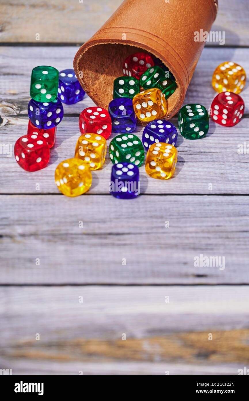 View to different colored game dices and a dice cup on a wooden table ...