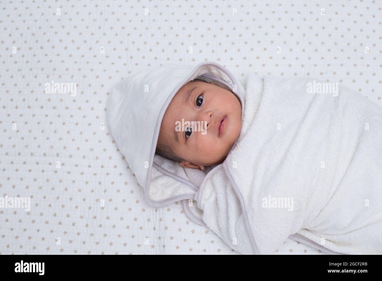 A cute newborn Malaysian baby girl lying on a bed wrapped in a white ...
