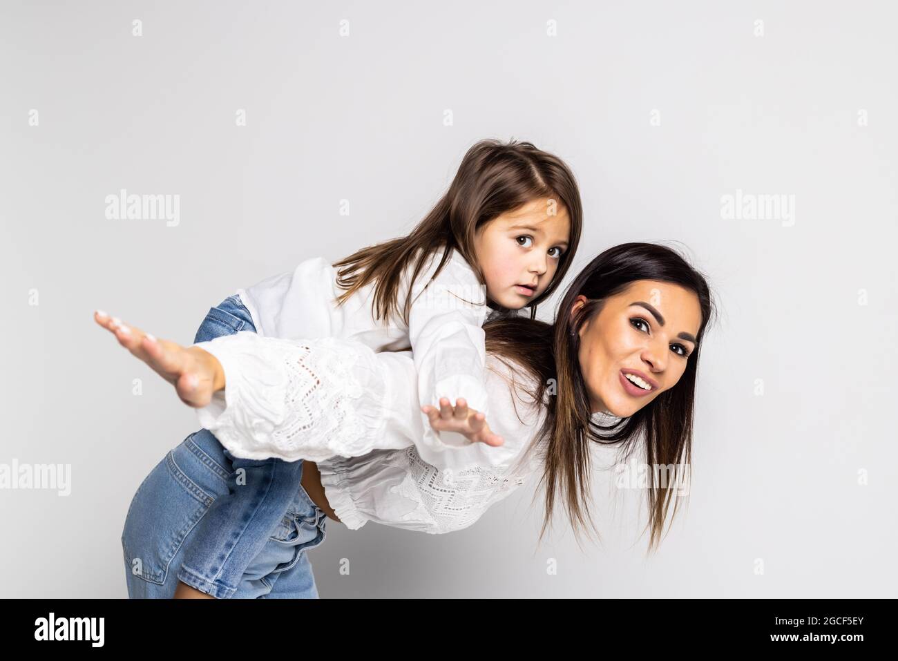 Mother giving her little daughter piggyback ride against white ...