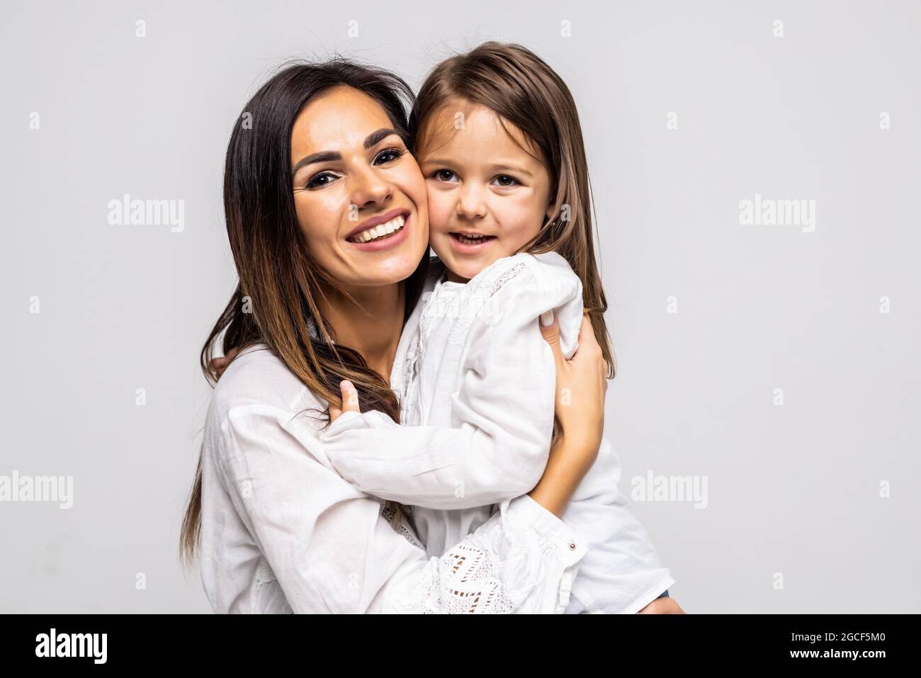 Happy beautiful young mother hug her little cheerful daughter on white background Stock Photo ...