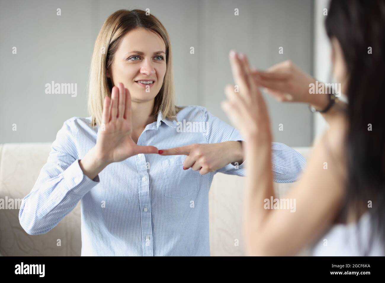 Two young happy women sitting on couch and making sign languages Stock ...