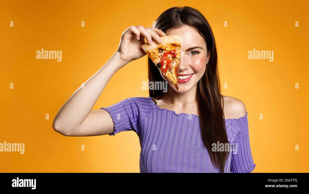 Beautiful modern girl showing slice of pizza near her face and smiling ...