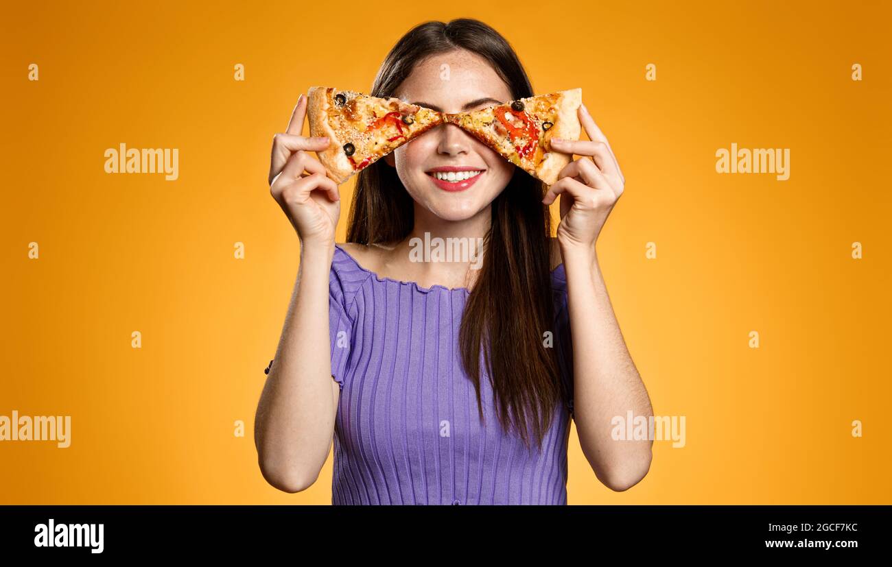Happy smiling young woman holding pizza slices on eyes with pleased ...