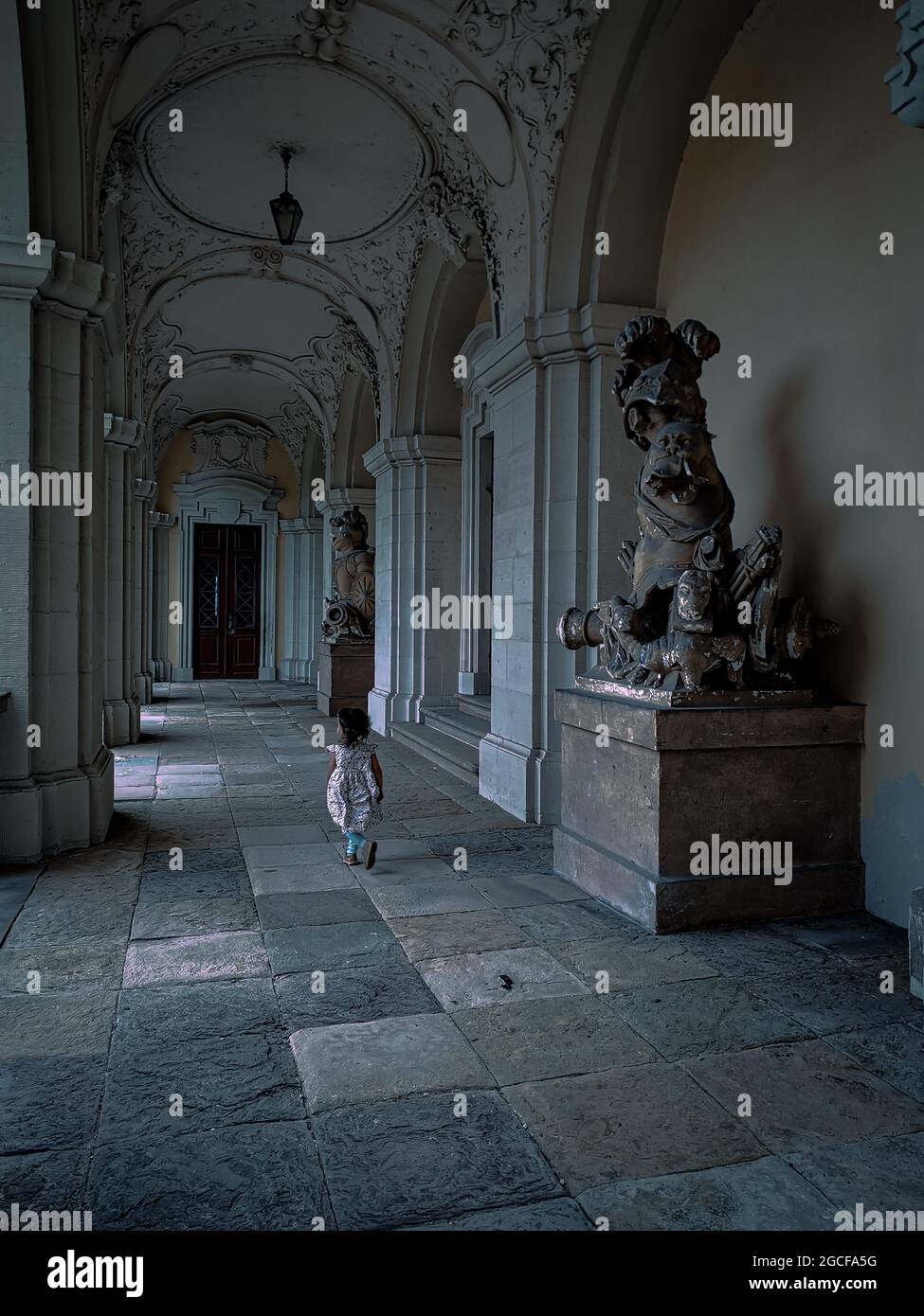 A little girl running in a corridor of an ancient castle with antique ...