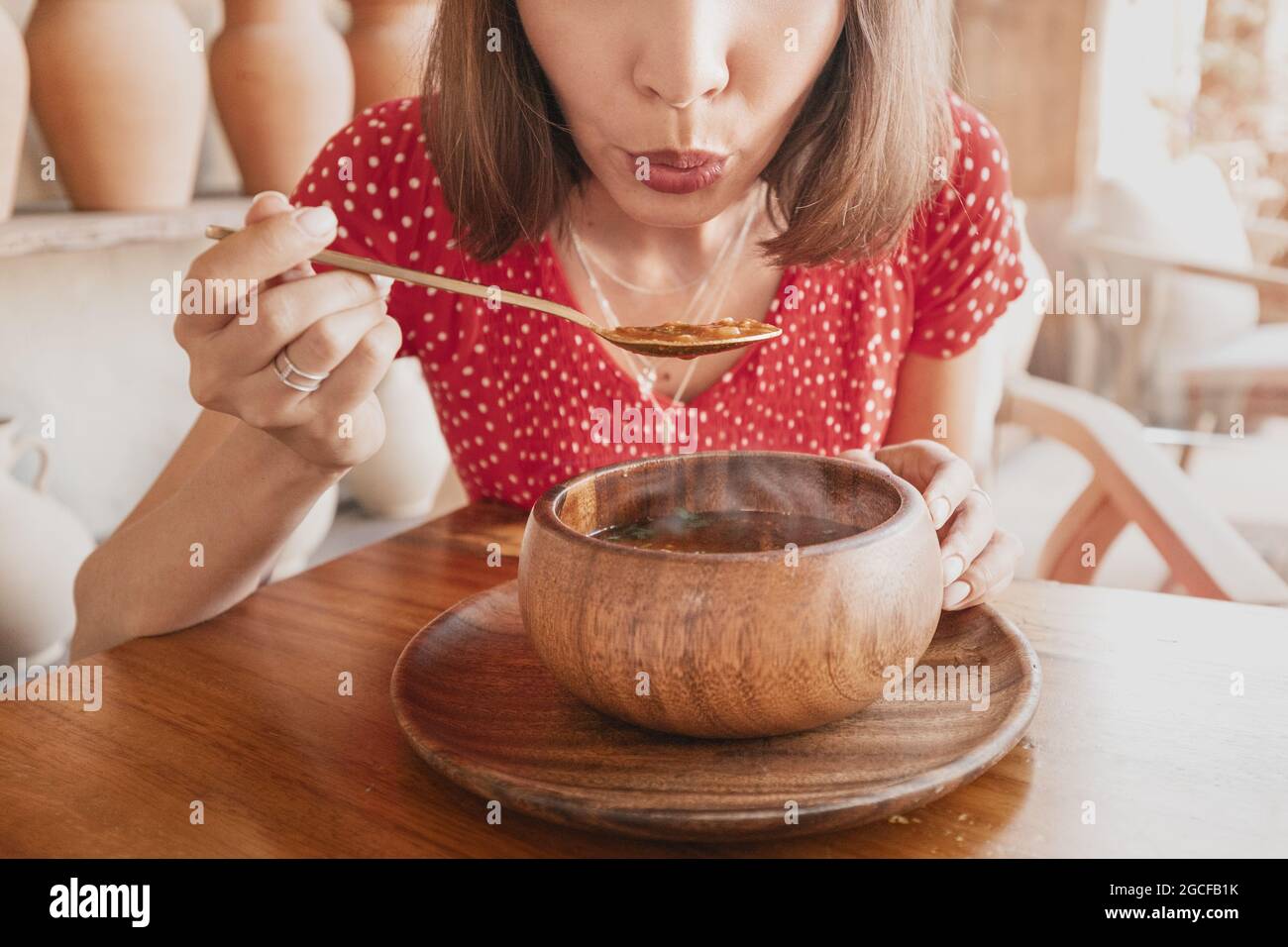 Asian woman eats chowder soup from a rustic wooden bowl in a restaurant ...