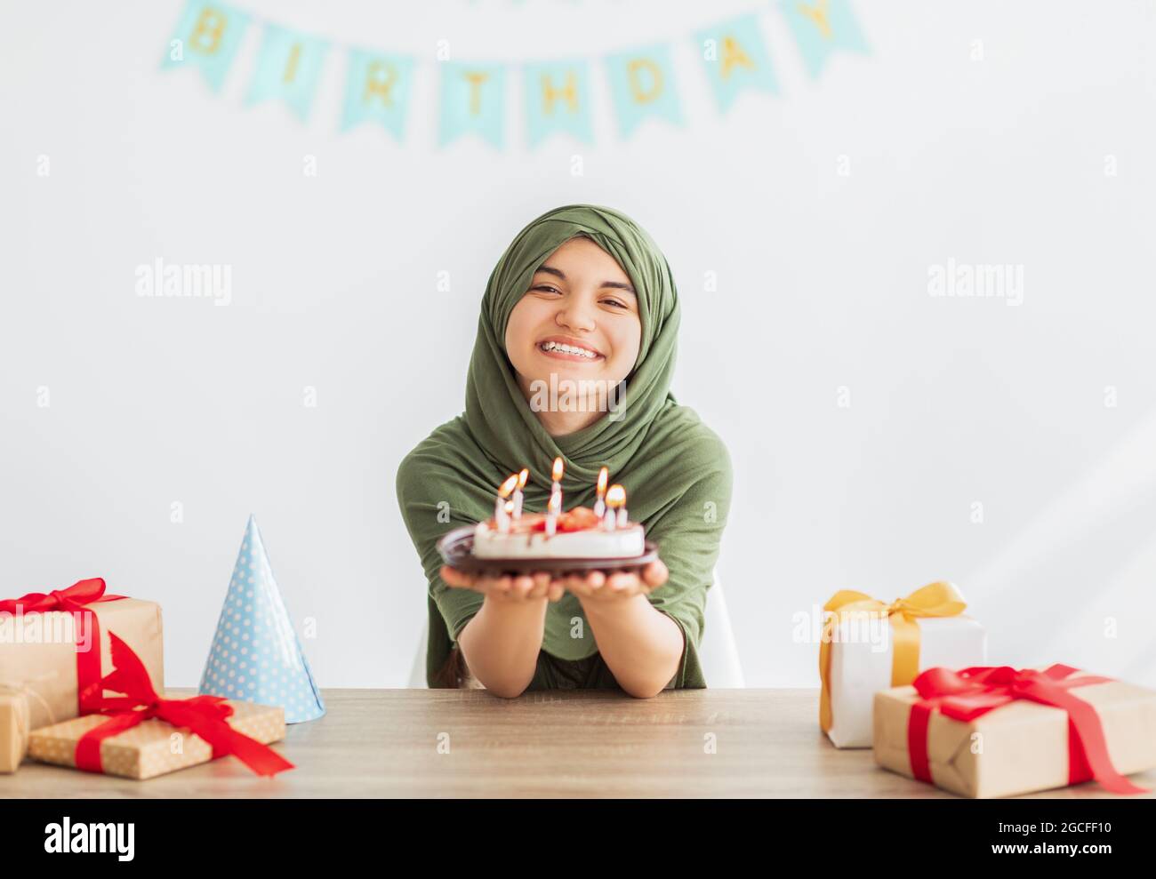 Muslim teen girl in hijab holding delicious birthday cake at table with ...