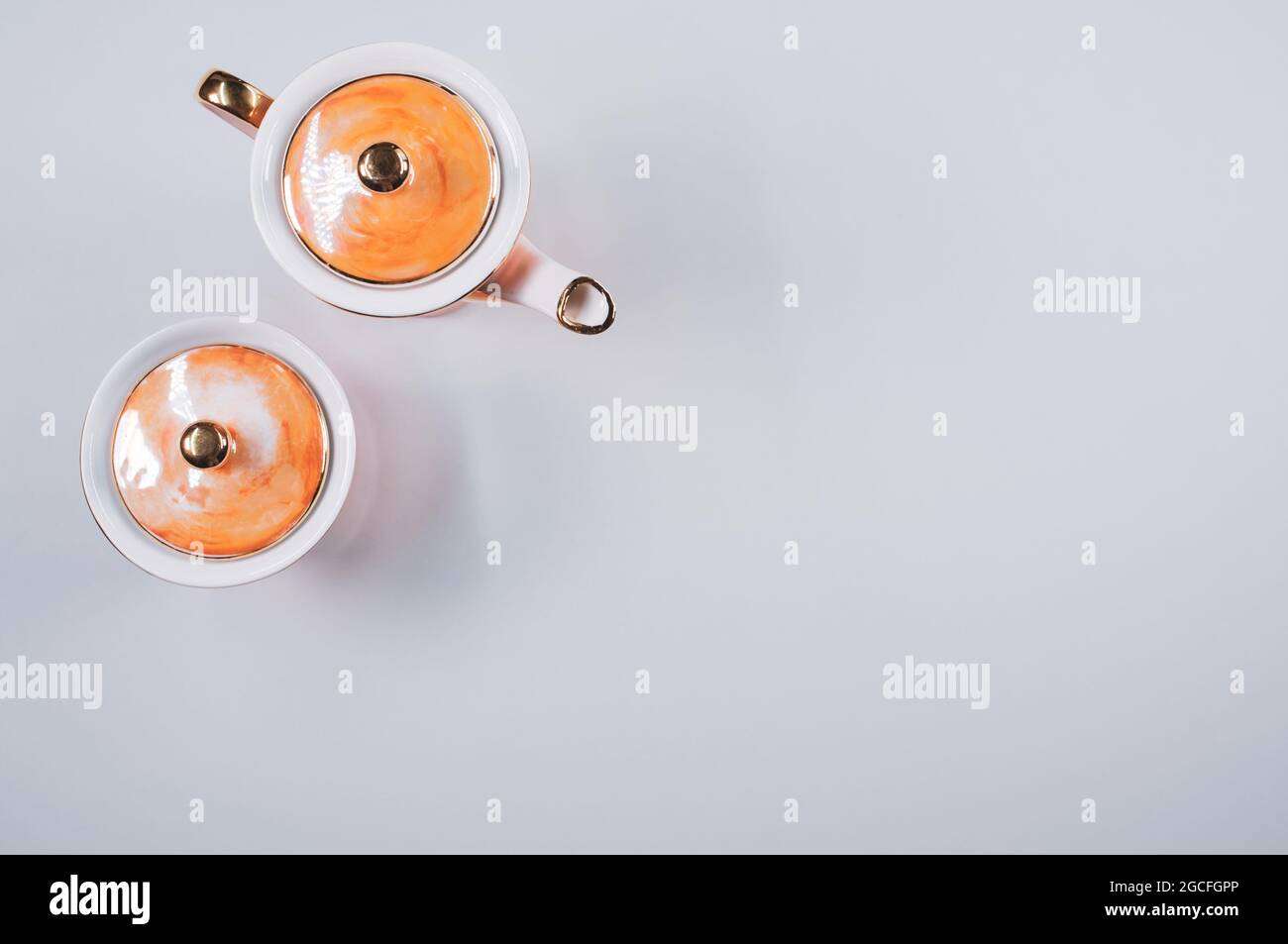 A top view of an orange covered teapot, a covered cup on an light isolated background with free ...