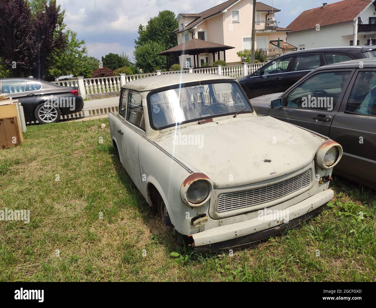 An old rusty vintage car parked in a garden surrounded by modern cars ...