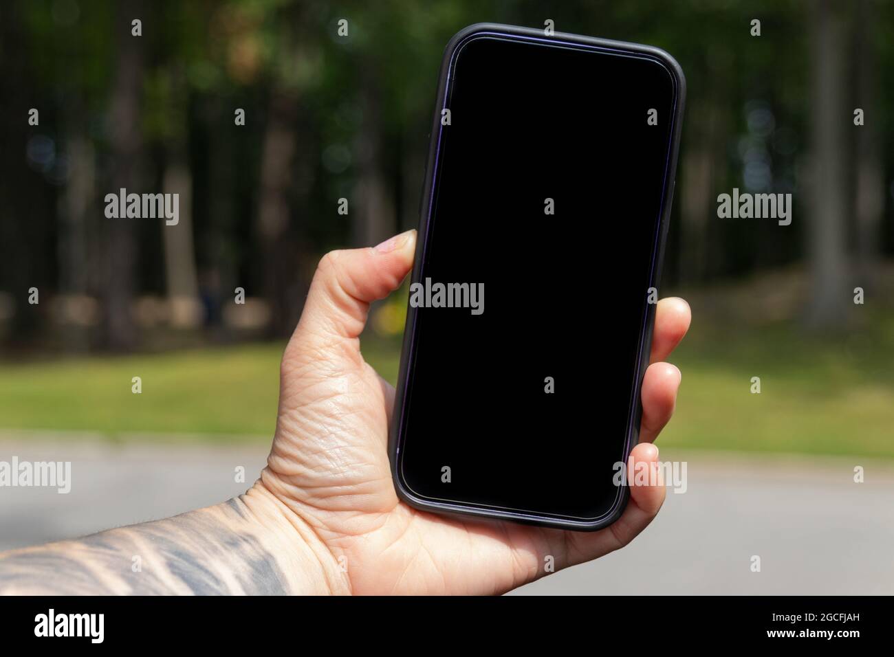 Tattooed wrist holding mobile phone outdoors with black blank screen ...