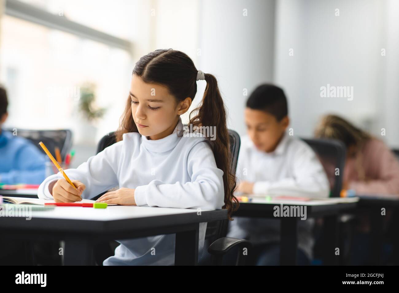 Tuition Concept. Portrait of concentrated small girl sitting at table ...