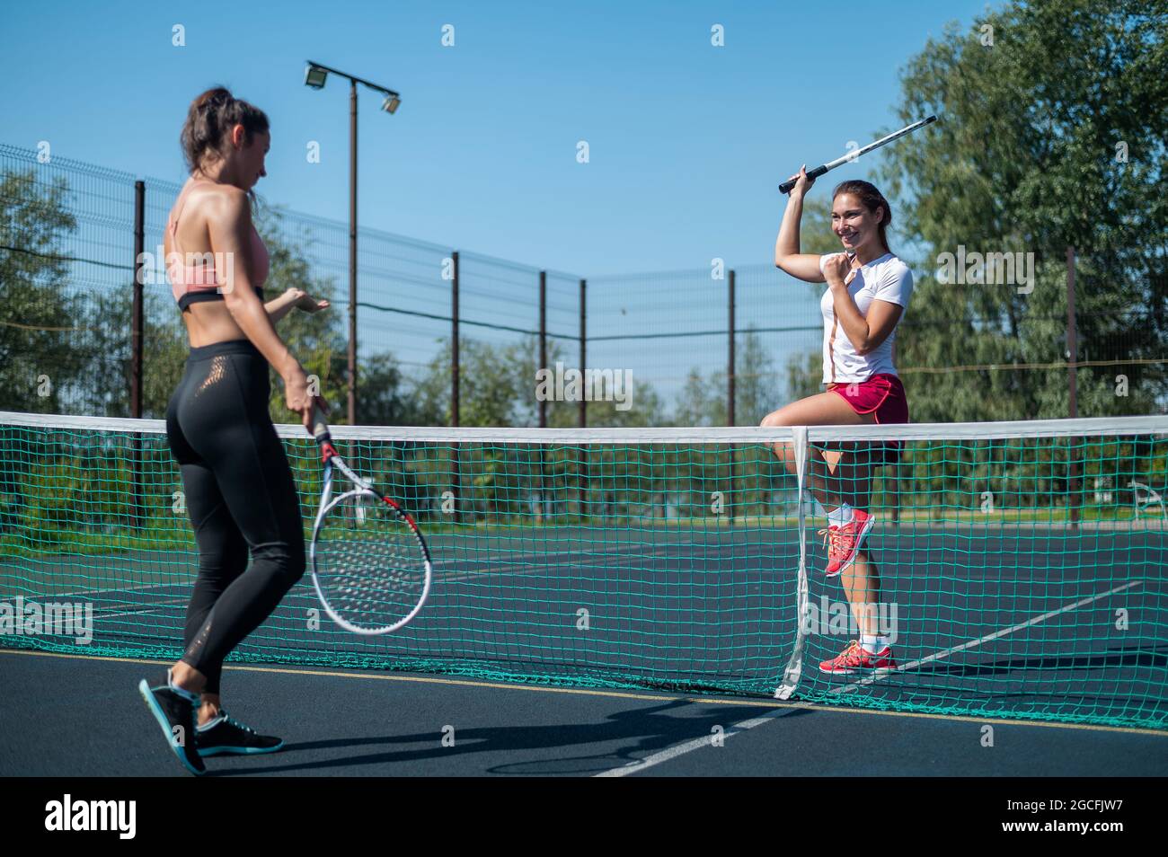 Two athletic young women play tennis on an outdoor court on a hot ...