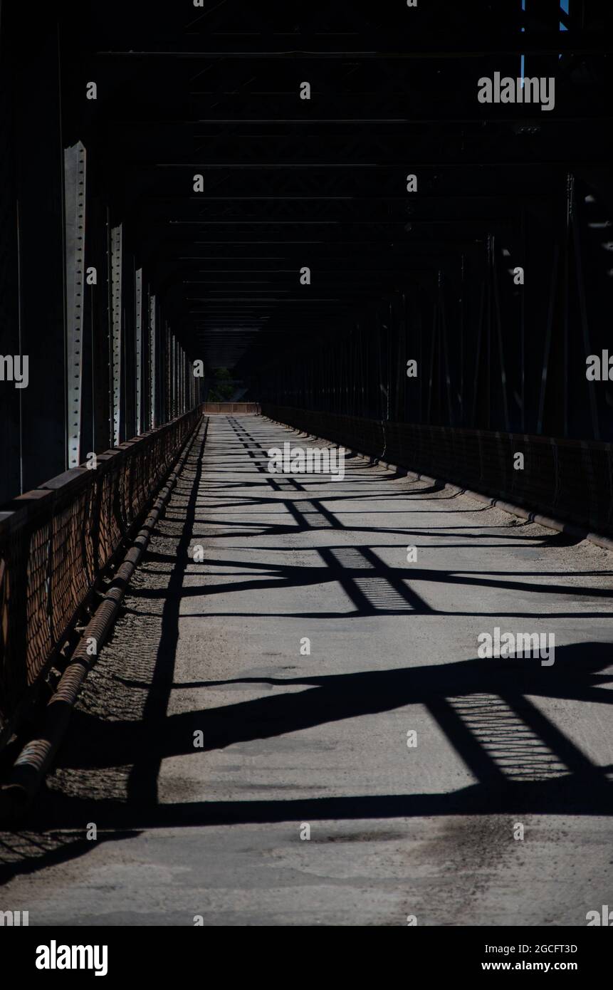 A vertical shot of a metal bridge at night with shadows falling on the ...