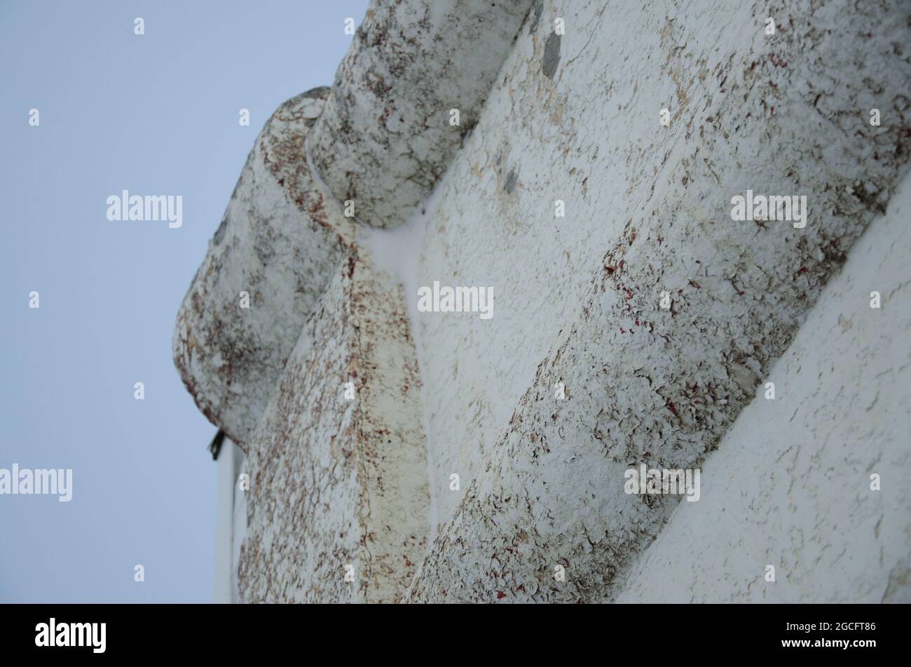 A closeup of a rusted white stone building under a blue sky with patchy ...