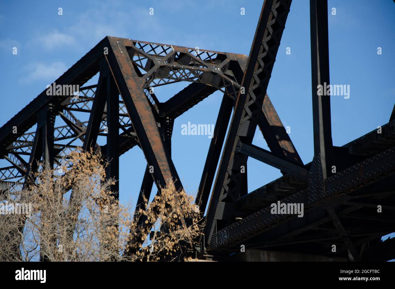 A closeup of an old rusted metal bridge under a bright blue sky with a ...