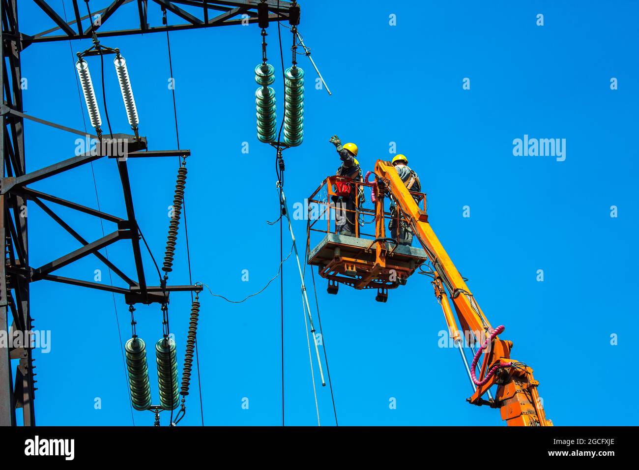 High voltage power line transmission tower workers with crane and blue ...