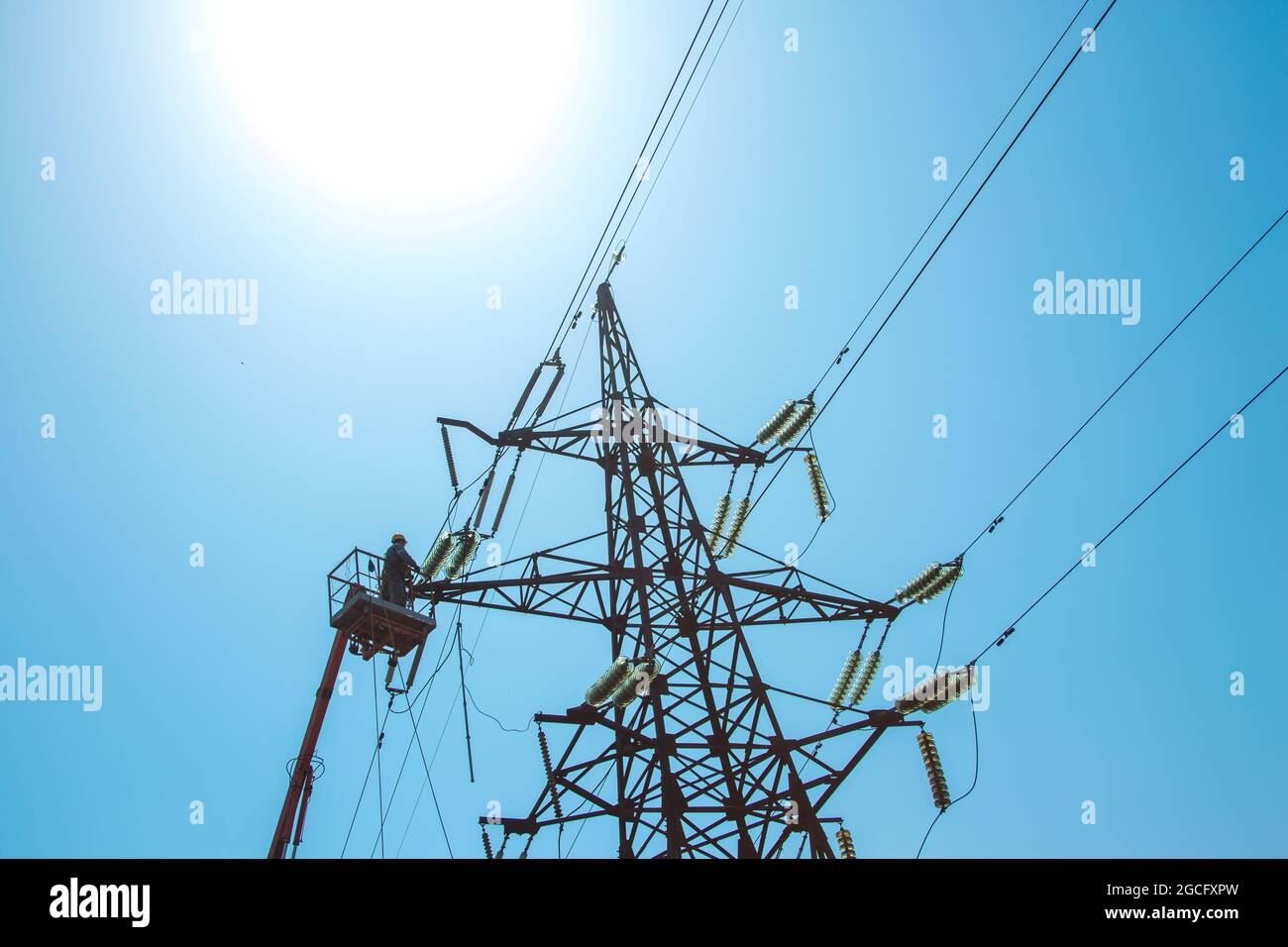 High voltage power line transmission tower workers with crane and blue ...