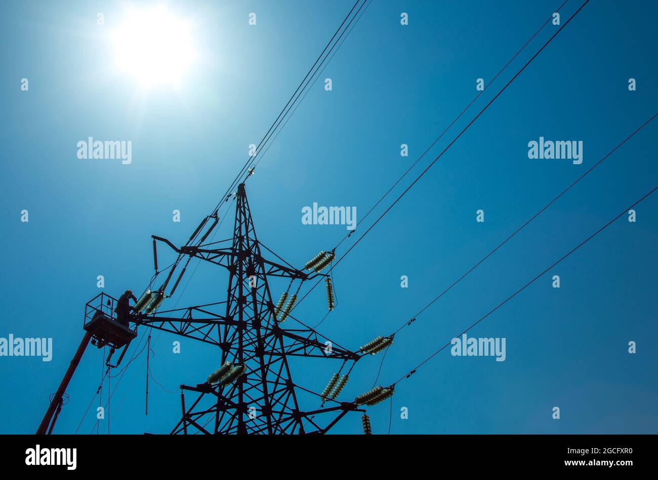 High voltage power line transmission tower workers with crane and blue ...
