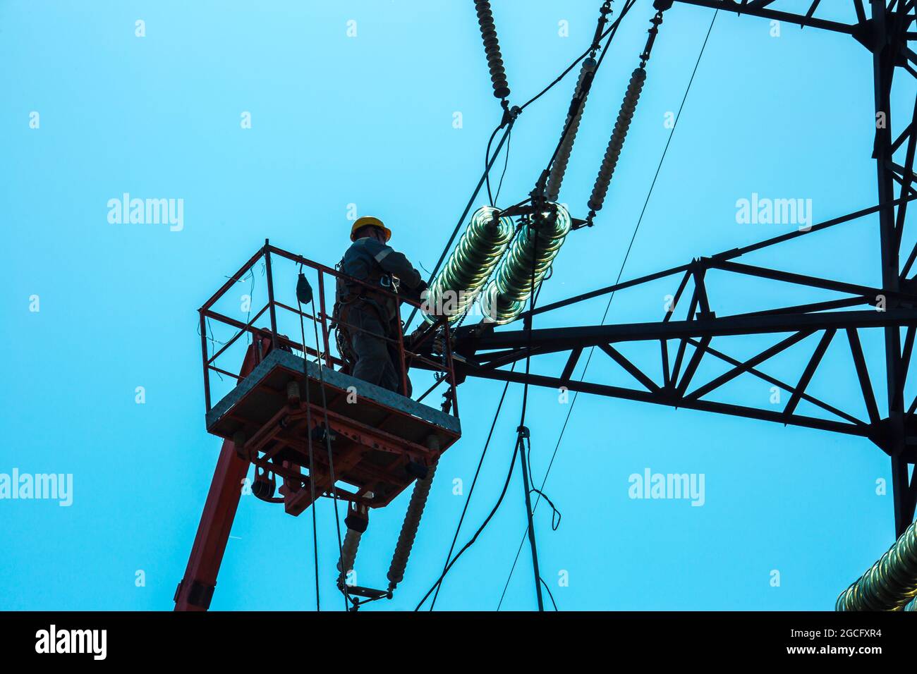 High voltage power line transmission tower workers with crane and blue ...
