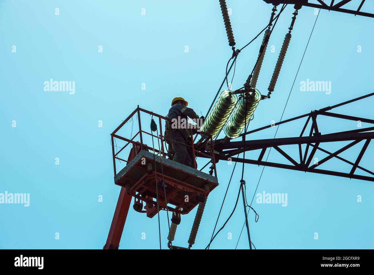 High voltage power line transmission tower workers with crane and blue ...