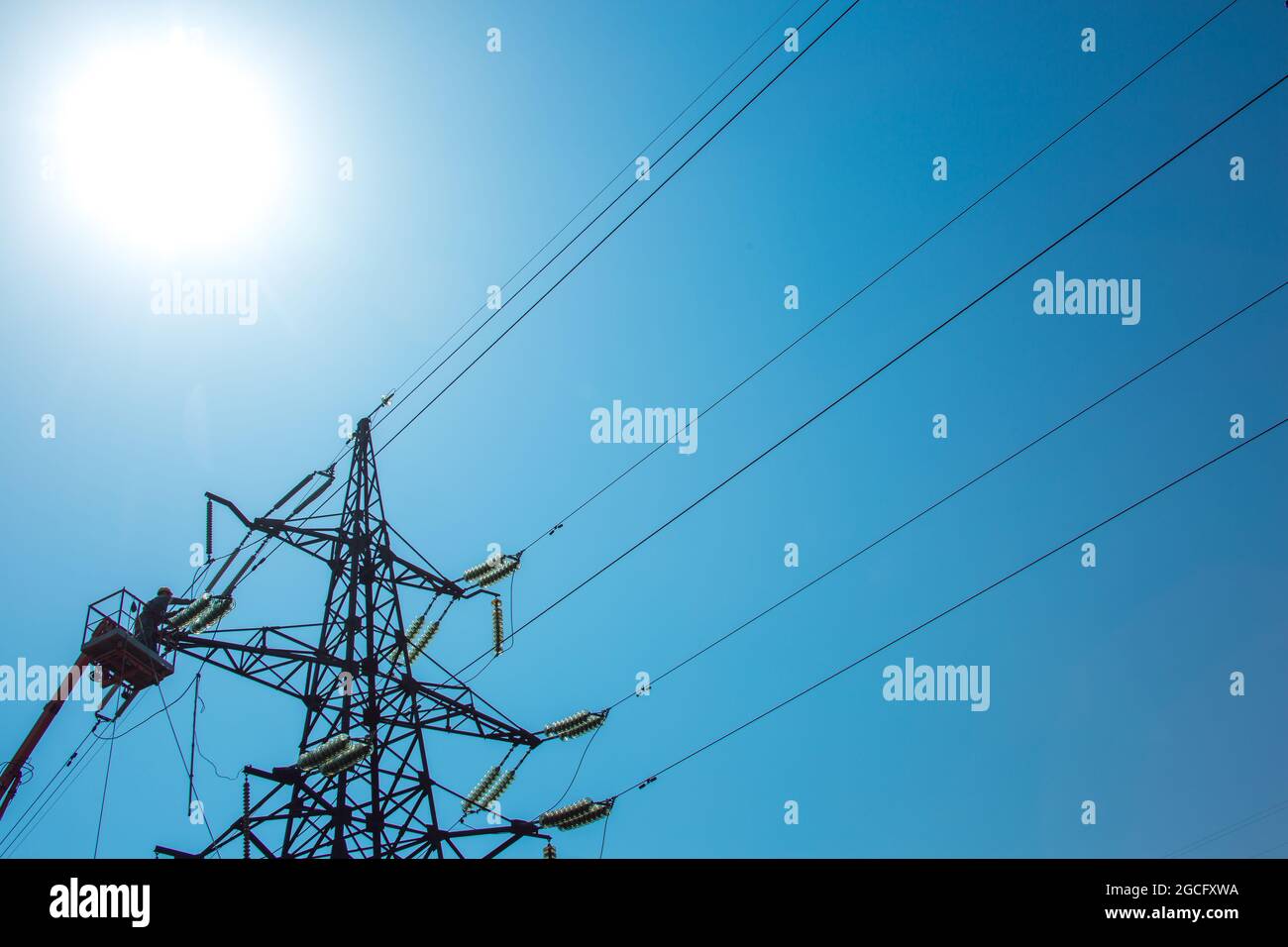 High voltage power line transmission tower workers with crane and blue ...