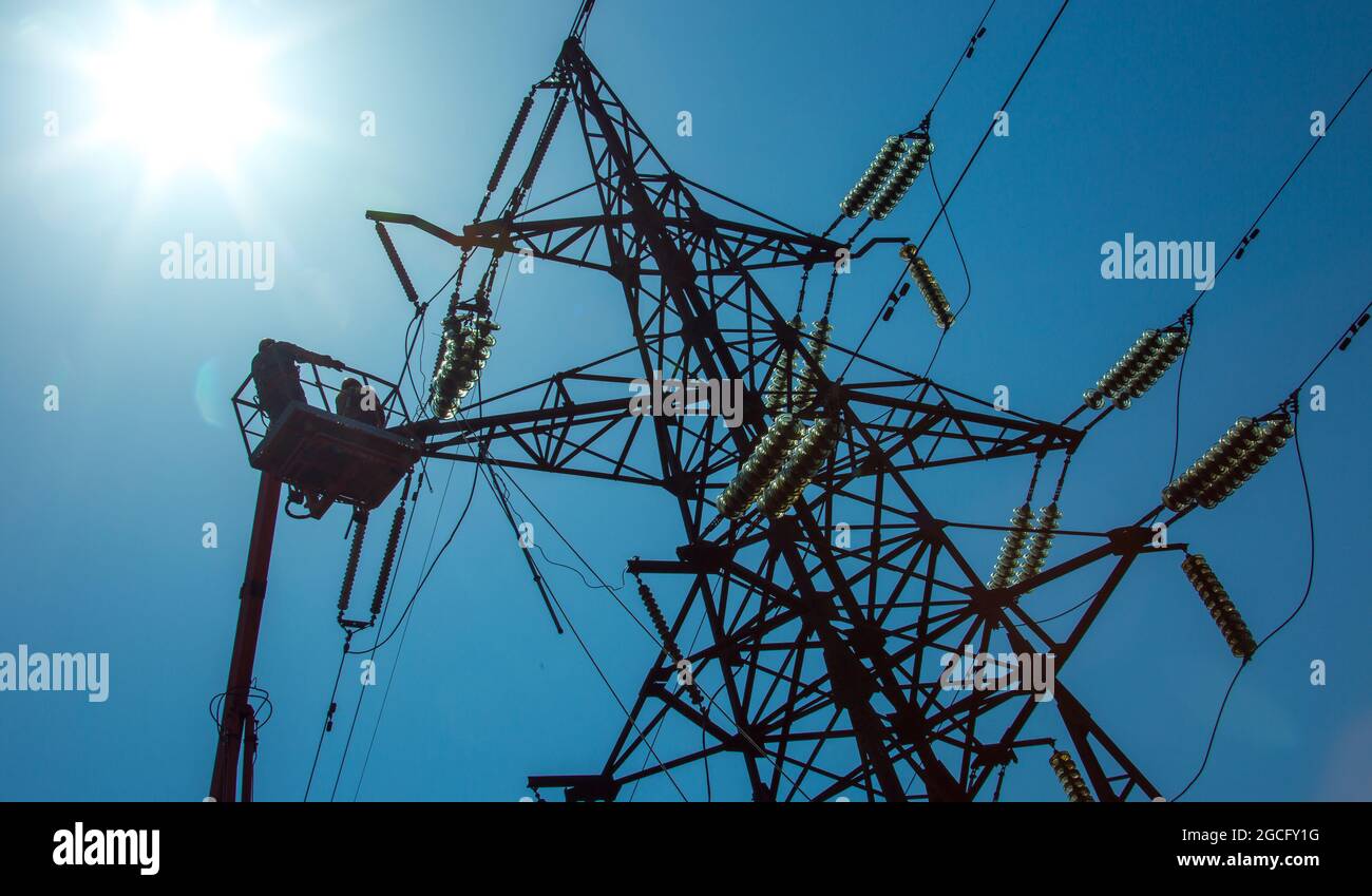High voltage power line transmission tower workers with crane and blue ...