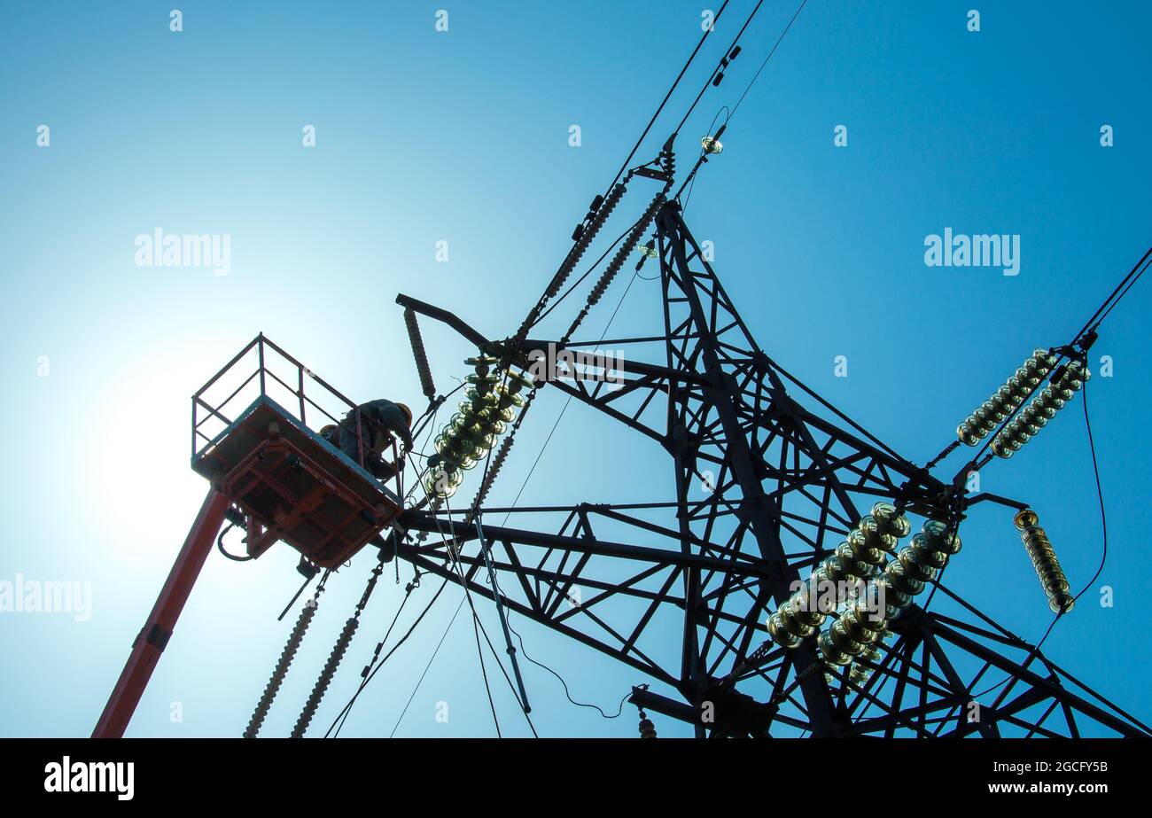 High voltage power line transmission tower workers with crane and blue ...