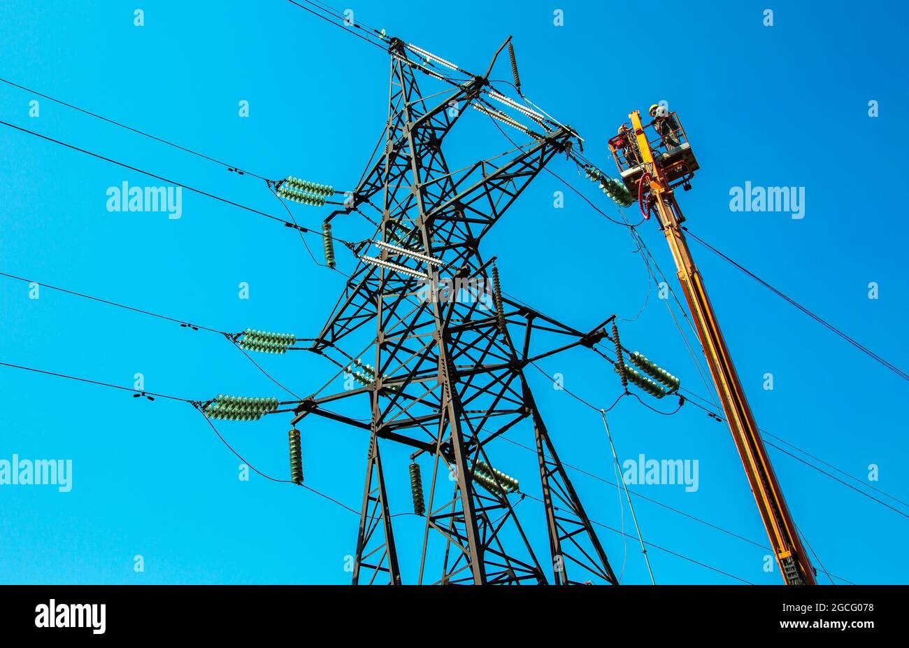 High voltage power line transmission tower workers with crane and blue ...