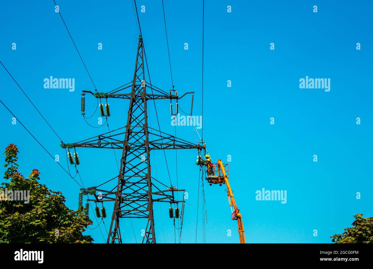 High voltage power line transmission tower workers with crane and blue ...