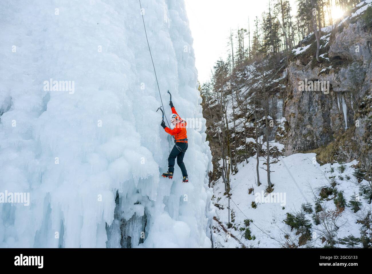 Aerial shot of a frozen waterfall, and a caucasian ice climber facing ...