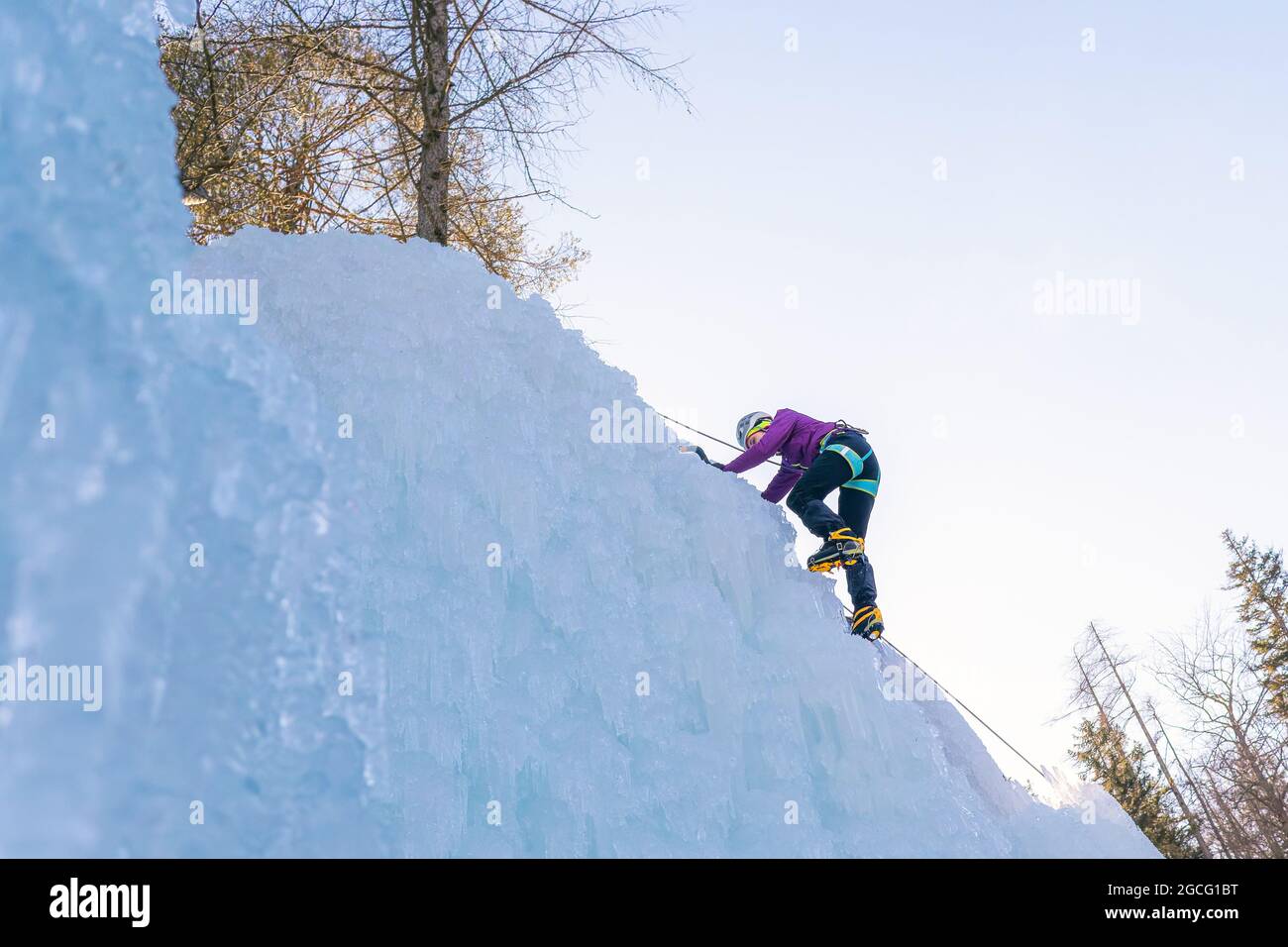 Female ice climber in traction position, swinging ice axes overhead and ...