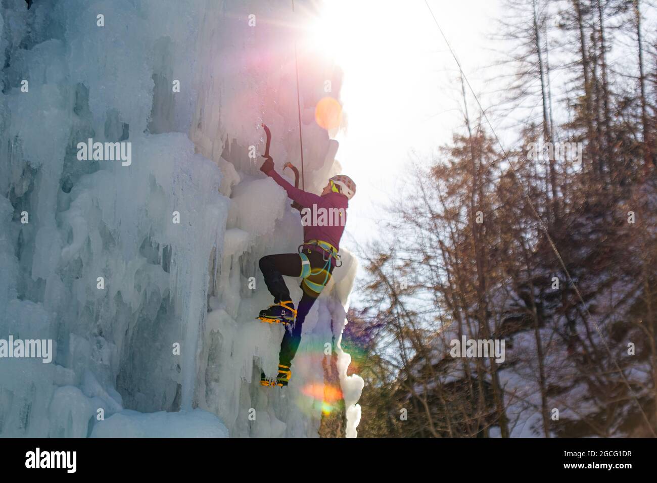Female ice climber hiking a frozen waterfall, pushing axe pick into the ...