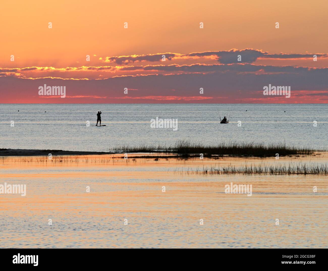 Silhouettes of a man on a surf board and a man in a kayak fishing on ...
