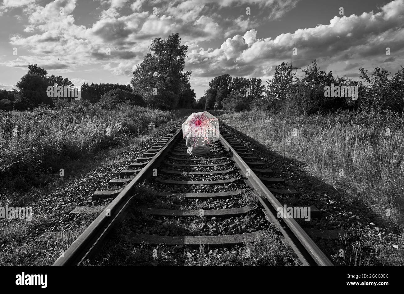 One person with a red umbrella is sitting on railway tracks in a black ...