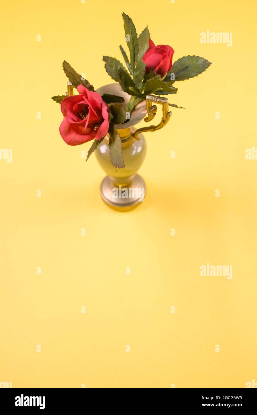A top view of red decorative roses in a small vintage vase on a yellow ...