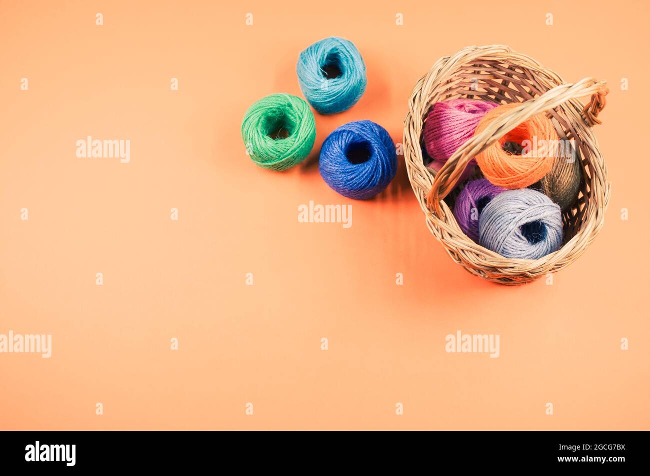 A pile of colorful textile balls of wool in a wicker basket on orange ...