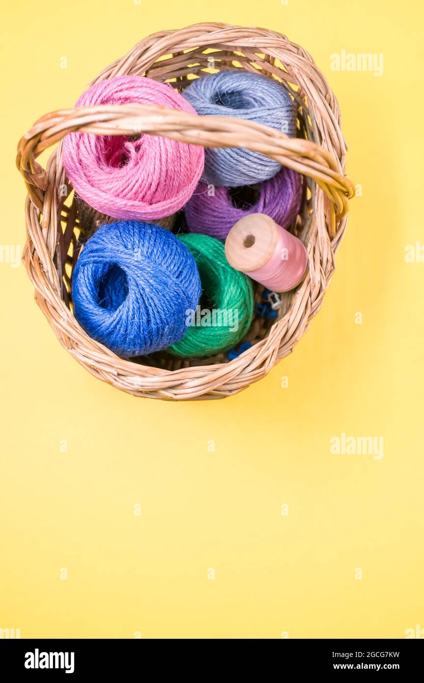 A pile of colorful textile balls of wool in a wicker basket on yellow ...