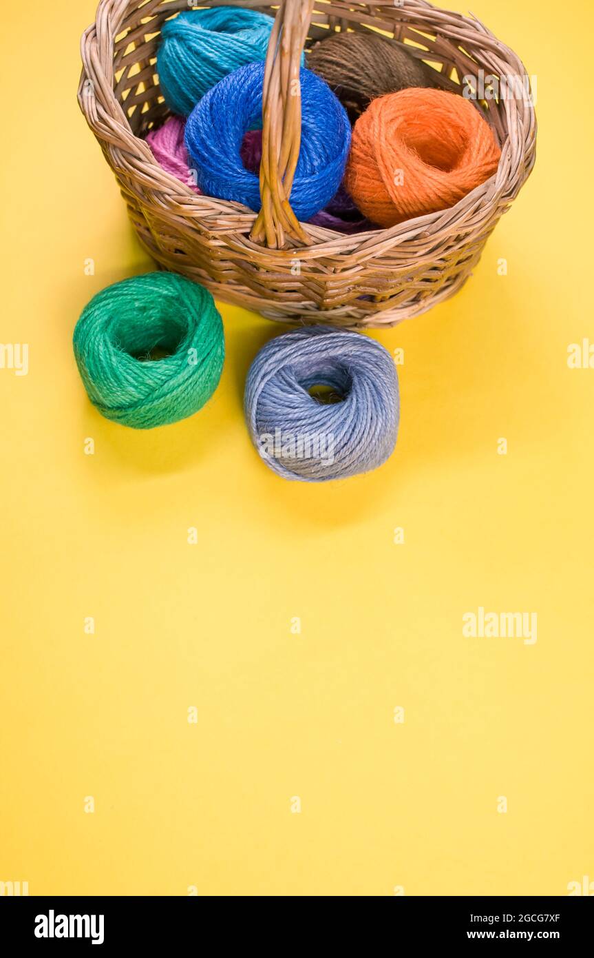 A pile of colorful textile balls of wool in a wicker basket on yellow ...