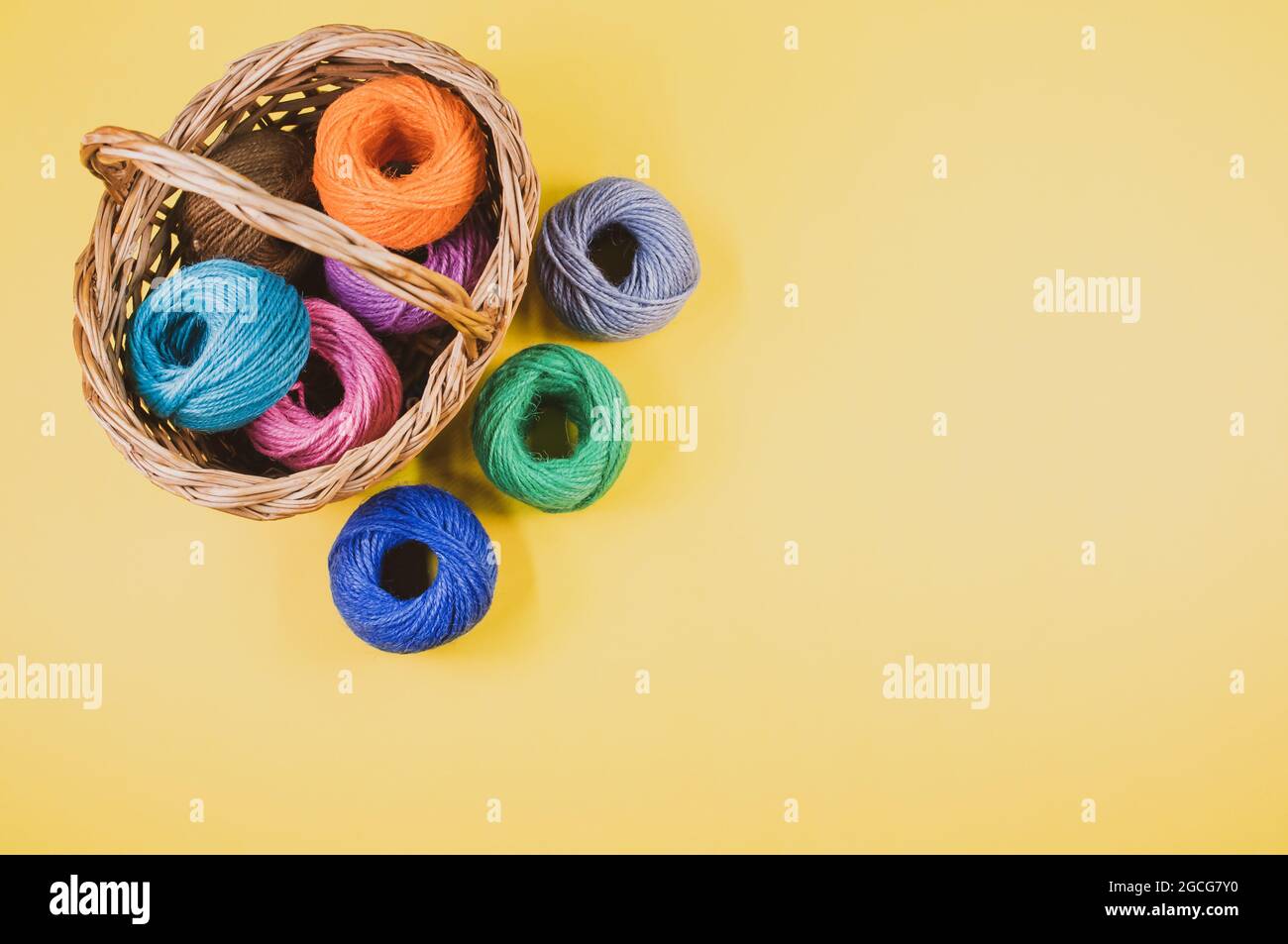 A pile of colorful textile balls of wool in a wicker basket on yellow ...
