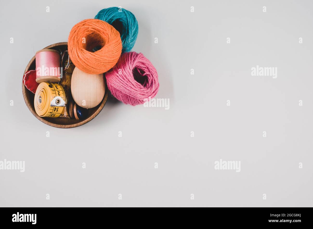 A bowl of sewing accessories and colorful textile balls of wool on gray ...