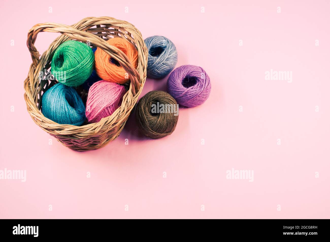 A pile of colorful textile balls of wool in a wicker basket on pink ...