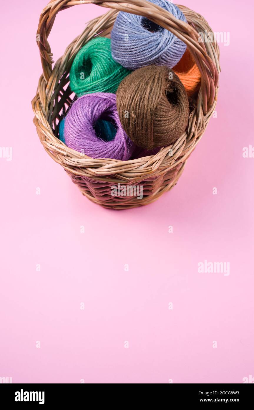 A pile of colorful textile balls of wool in a wicker basket on pink ...