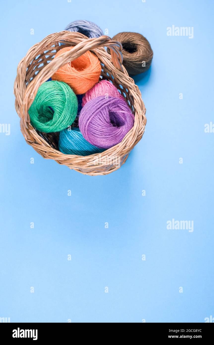 A pile of colorful textile balls of wool in a wicker basket on blue ...
